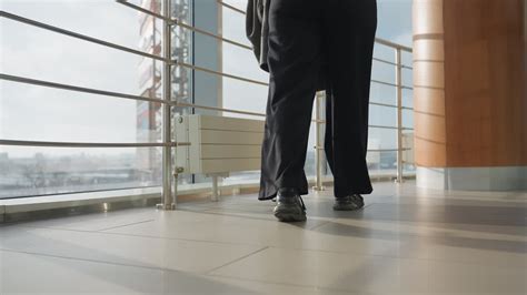 Low Angle Rear View Of Person In Black Pants And Sneakers Walking Across Tiled Indoor Floor