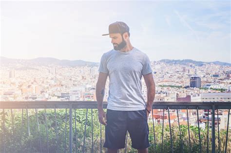 Hipster 캐주얼 스포츠 도시 스타일에 회색 공백 T셔츠와 귀하의 로고 또는 디자인에 대 한 공간을 가진 검은 Snapback 모자를 착용 하는 수염과 잘생긴 남성 모델