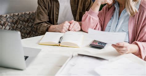 노인 배우자는 집에서 부엌에 앉아 예산을 계획하면서 테이블에서 청구서 수표 컴퓨터 문서 및 계산기를 확인합니다 잘린 개념