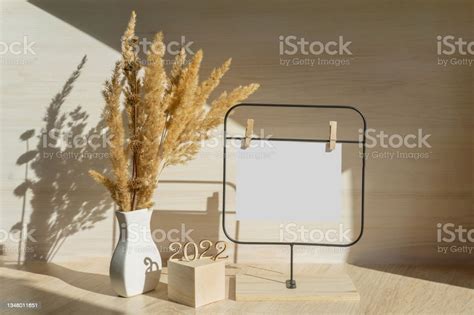 베이지 색 나무 작업 테이블에 말린 잔디와 흰색 꽃병 숫자 2022와 3d 연단 햇빛의 광선에 종이의 빈 시트와 함께 서 에키바나 옆에 위치하고 있습니다 메모장에 대한 스톡