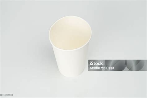 평평한 표면에 황색을 띤 액체가 담긴 중앙의 1인분 스티로폼 컵 위에서 오는 광원은 부드러운 그림자와 내부 빛을 만듭니다 설명할 수 없는 배경은 컵에 주의를 집중시킵니다