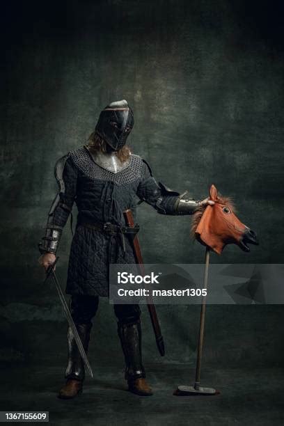 헬멧과 갑옷을 타고 장난감 말을 입고 어두운 배경에 고립 된 큰 칼을 들고 중세 전사 또는 기사의 초상화 시대 역사의 비교 기사 사람의 역할에 대한 스톡 사진 및 기타