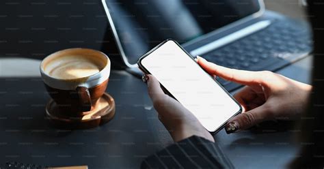 컴퓨터 노트북과 커피 컵이 테이블 위에 놓인 흰색 빈 화면이 있는 자른 검은색 스마트폰을 들고 있는 임원 여성의 손이 자른 이미지 사진 Unsplash의 휴대폰 이미지