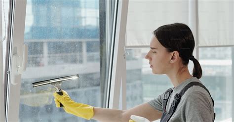 젊은 여성 클리너는 창문에 세제를 뿌리고 대형 오픈 스페이스 사무실에서 일하는 동안 특수 실리콘 주걱으로 문지릅니다 사진 Unsplash의 성인 이미지