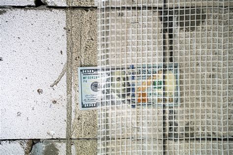 폭기 된 콘크리트 벽돌 벽 클로즈업에 투명한 강화 필름 뒤에 숨겨진 100 달러 수증기 장벽은 벽에 붙어있는 돈을 덮습니다 금융 및 건설 건설 산업에 대한 스톡 사진 및