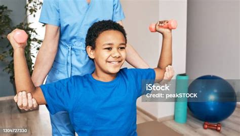 아프리카계 미국인 소년은 재활 센터에서 아령을 사용하여 물리 치료사와 함께 훈련합니다 아령을 사용하여 손을 들고 미소 짓는 아이