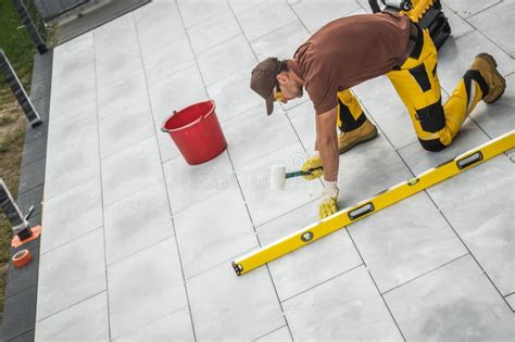 A Worker Carefully Lays Tiles Using A Level Tool On A Clean Outdoor