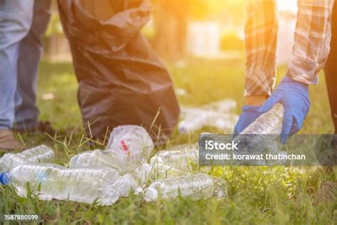 두 명의 직원이 검은색 쓰레기 봉투를 사용하여 잔디밭과 보도에서 플라스틱 병과 재활용 가능한 폐기물을 수거하여 재활용합니다 재활용을 위한 플라스틱 폐기물 분류의 개념 2명에