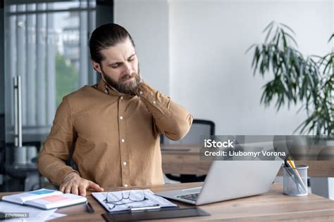 나무 책상 위에 문서와 안경을 놓고 현대적인 사무실 환경에서 노트북으로 작업하는 동안 목에 불편함을 겪고 있는 사업가 인체공학에