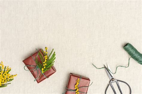 빨간색 공예 종이의 선물 상자는 테이블 베이지 색 식탁보에 천연 미모사 꽃을 장식했습니다 봄 휴가 선물 포장 아늑한 Diy 선물 플랫 레이 복사 공간이 있는 상위 뷰 배경