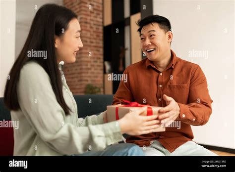 Loving Young Asian Wife Giving Present To Her Happy Mature Husband
