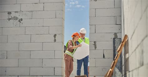 웃는 금발 아가씨와 보호 헬멧과 반사 조끼를 입은 남자가 집 계획을 응시하고 있다 사진 Unsplash의 건축 계약자 이미지