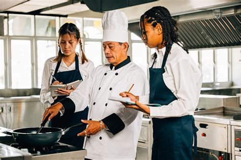 식당 주방에서는 아시아인 선임 셰프가 다인종 학생들에게 요리 기술을 전수합니다 이 교육 워크숍에서는 팀워크 학습과 필기에 중점을 둡니다 음식 도크 14 15 살에 대한 스톡