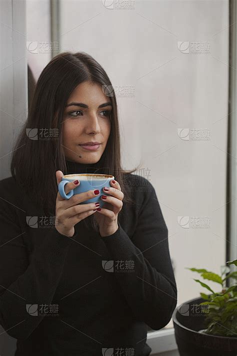年轻女子坐在窗边沉思着喝咖啡