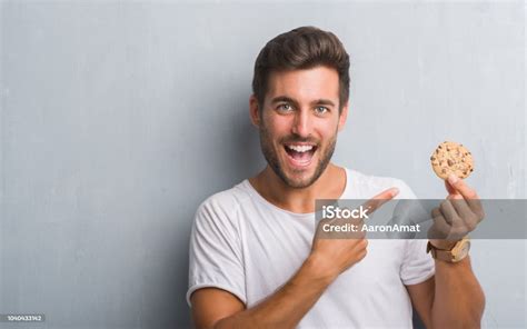 그런 지 회색 벽 먹는 초콜릿에 잘생긴 젊은 남자 칩 과자 손과 손가락으로 가리키는 매우 행복 남자에 대한 스톡 사진 및 기타 이미지 Istock