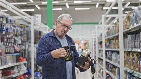 An Elderly Man In An Auto Shop Chooses A Car Compressor Compares Two