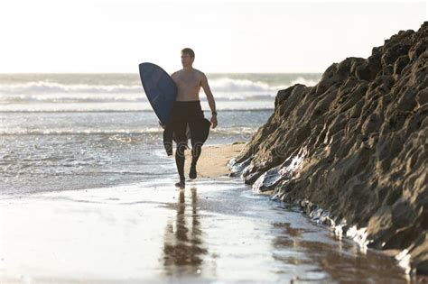 Un Hombre Con Un Torso Desnudo Caminando Por La Playa Con Una Tabla De Surf Imagen De Archivo