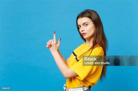 스튜디오에서 밝은 파란색 배경에 고립 된 총 처럼 손을 잡고 카메라를 찾고 생생한 캐주얼 옷에 자신감 아름 다운 젊은 여자의 측면도 사람들 라이프 스타일 개념입니다 복사