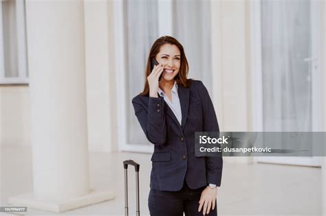 젊은 웃는 백인 사업가 야외에서 스마트 캐주얼 서와 스마트 폰을 사용 하 여 옷을 입고 그녀 옆에는 짐이 있습니다 가방에 대한 스톡 사진 및 기타 이미지 Istock