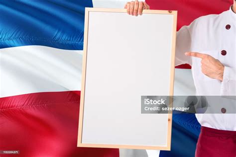 도미니카 공화국의 국기 배경에 빈 화이트 보드 메뉴를 들고 있는 도미니크 요리사 텍스트에 대 한 균일 한 포인팅 공간을 착용 요리 고급 요리에 대한 스톡 사진 및 기타