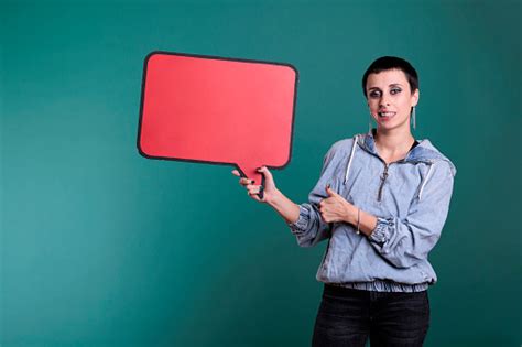 짧은 머리를 가진 갈색 머리 여자는 스튜디오에 서 있는 빈 빨간 말풍선을 가리키고 있다 기포에 대한 스톡 사진 및 기타 이미지 기포 대화 풍선 문자 기호 루마니아