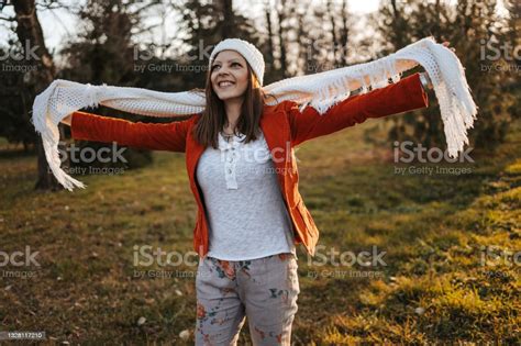 오렌지 색 재킷과 흰색 모자와 스카프를 입은 초상화 유행의 아름다운 젊은 여성 가을에 공공 공원에 서서 멀리 보고 가을에 대한