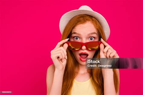 좋은 매력적인 사랑 스러운 사랑 스러운 충격된 빨간 머리 여자 긴 황금 머리를 가진 착용 모자 퍼 팅 아래에 고립 된 밝고 선명한 적자 색 배경 색 안경의 클로즈업 초상화