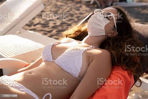해변에서 하얀 보호 얼굴 마스크와 수영복을 입고 일광욕을 하는 소녀 보호 마스크에 대한 스톡 사진 및 기타 이미지 보호 마스크 바다 일광욕 Istock