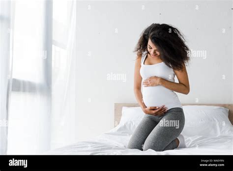 Happy African American Pregnant Woman Touching Belly While Sitting On
