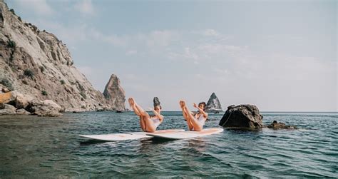 여자는 요가를 한다 패들 섭 서핑보드에서 요가 필라테스를 연습하는 행복한 스포티한 여성 바닷물에서 운동을 하는 여성 스트레칭 현대 개별 여성 힙스터 야외 여름 스포츠 활동