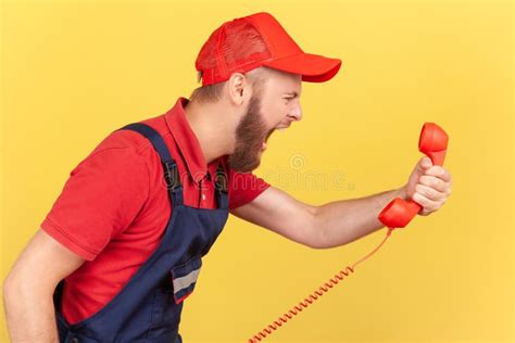 aggressive worker wearing blue overalls screaming to client on handset