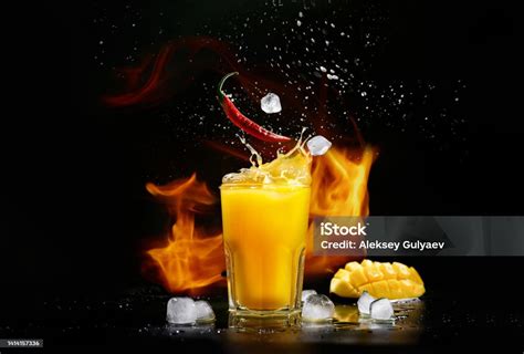 카모마일 소스와 칠리 라임 향신료를 곁들인 Mangonada 멕시코 망고 스무디 검은 배경에 망고와 칠리 후추 칵테일 얼음 조각은 망고나다가있는 유리에 떨어집니다 고추류에