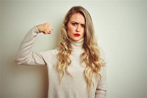 고립 된 흰색 배경 위에 겨울 터틀넥 스웨터를 입은 아름다운 여성은 팔 근육을 보여주는 강한 사람 자신감과 힘을 자랑스럽게