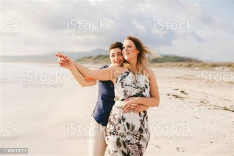 사랑에 젊은 부부는 서로 포옹하고 그들 중 하나는 여름 저녁에 황량한 해변에 포인트를 나타냅니다 2명에 대한 스톡 사진 및 기타 이미지 Istock