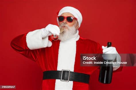 은퇴 한 노인 회색 수염 펑키 한 보류 병 전체 유리 황금 와인 음료 재미 열린 입 착용 산타 Xmas 복장 멜빵 선글라스 모자