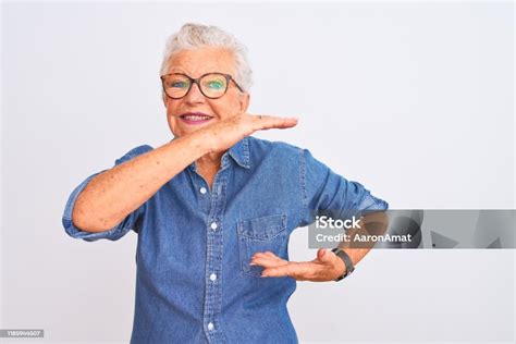 데님 셔츠와 안경을 쓰고 있는 시니어 그레이헤어 여성은 크고 큰 크기의 간판을 보여주는 손으로 하얀 색 배경에 몸짓을 하고 상징을 측정합니다 카메라를 바라보며 웃고 있습니다