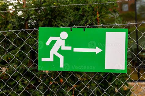 A Green Exit Sign With A White Stick Figure Running Right Is Attached To A Chain Link Fence