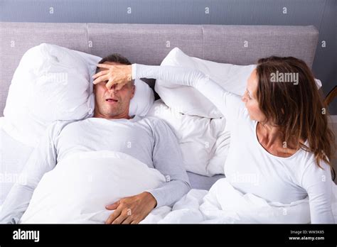 Frustrated Matured Woman Trying To Stop Mans Snoring With Her Finger While Sleeping On Bed
