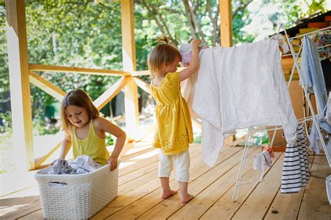 소녀 자매는 집안일을 돕고 아이들은 세탁을 위해 바닥 건조기에 플라스틱 바구니에서 씻은 세탁물을 걸어 놓고 집 근처 뒤뜰에서 여름에는 2 3 살에 대한 스톡 사진 및 기타