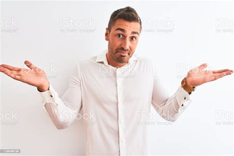 고립 된 배경에 우아한 셔츠를 입고 젊은 잘 생긴 사업가는 팔과 손을 들고 단서와 혼란스러운 표정을 짓고 있습니다 의심 개념