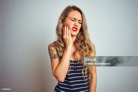 치통이나 치아 질환으로 인해 고통스러운 표정으로 입을 만지는 흰색 고립 된 배경 위에 서있는 줄무늬 티셔츠를 입은 젊은 아름다운 여성 치과 의사 개념 T 셔츠에 대한 스톡