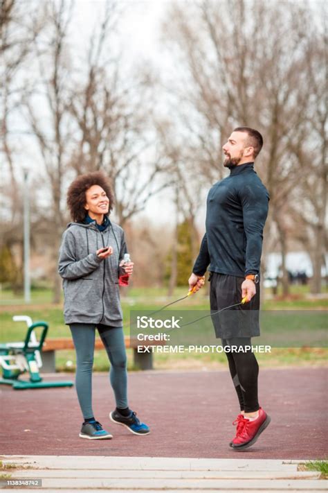 그 옆에 서 있는 여성 피트 니스 강사와 함께 공원에서 점프 로프 운동을 하 고 스톱 워치와 시간을 측정 하는 강한 운동 남자 2명에 대한 스톡 사진 및 기타 이미지