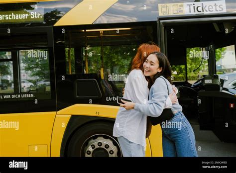 Young Cute Smiling Asian Girl Hugging Her Beautiful Redhead Friend Near Bus With Opened Door