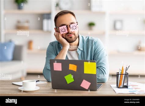 Tired Young Man Having Stickers With Open Eyes Drawing On Glasses Sleeping Near Laptop
