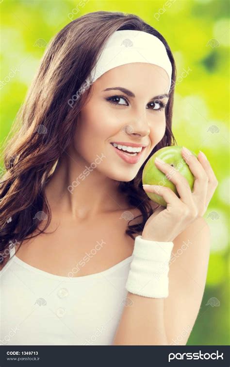 زن جوان خندان شاد با لباس ورزشی با سیب سبز در فضای باز 1349713