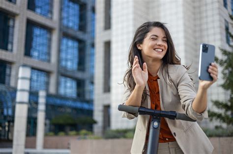스마트폰을 들고 있는 여성 기업가들이 도시 거리의 비즈니스 센터 근처에서 전기 푸시 스쿠터를 운전하고 있다 교통 환경 개념