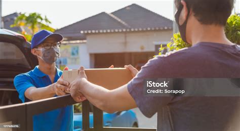 아시아 젊은 배달 남자 택배 와 패키지 우편 상자 에 균일 한 그는 보호 얼굴 마스크 그는 서비스를 만들고 고객 수신 전면 집 에서 통행 금지 검역 전염병 전염병 코로나