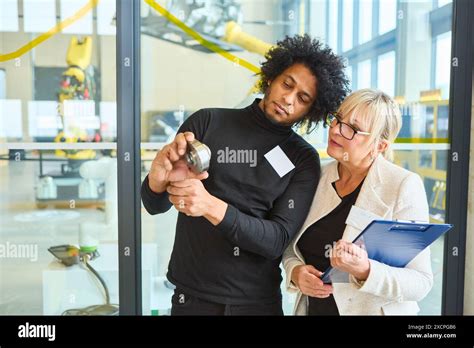 Two Engineers Closely Examine A Robotic Gripper Part In An Industrial