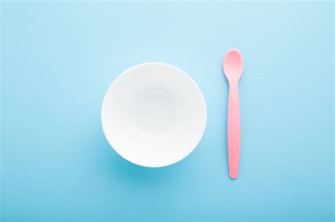밝은 파란색 테이블 배경에 흰색 그릇과 분홍색 플라스틱 숟가락 파스텔 색상 근접 촬영 아기 요리 하향 보기 0명에 대한 스톡