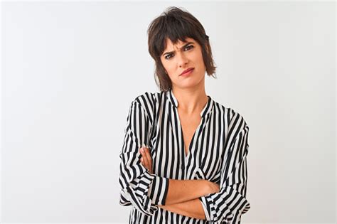 고립 된 흰색 배경 회의론자 및 긴장 위에 서있는 줄무늬 셔츠를 입은 젊은 아름다운 여성은 교차 된 팔로 얼굴에 표정을 거부합니다 부정적인 사람 감정에 대한 스톡 사진 및